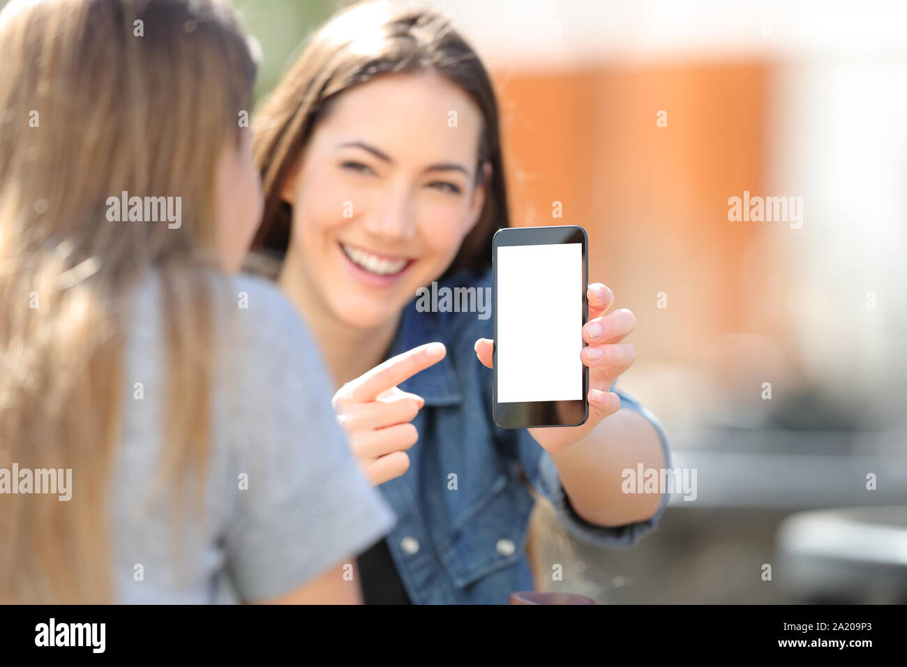 Happy girl shows blak smart phone screen to her friend in the street ...