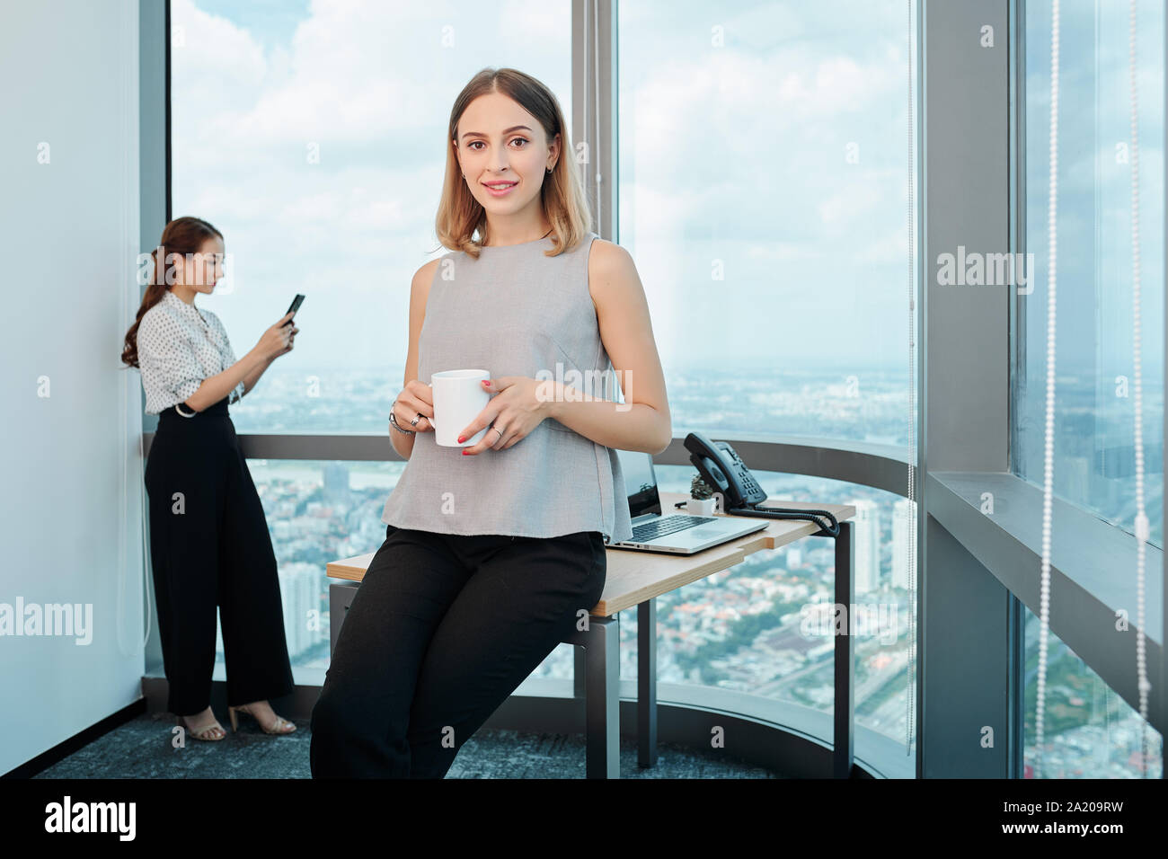 Portrait of pretty smiling female entrepreneur sitting on edge of her ...