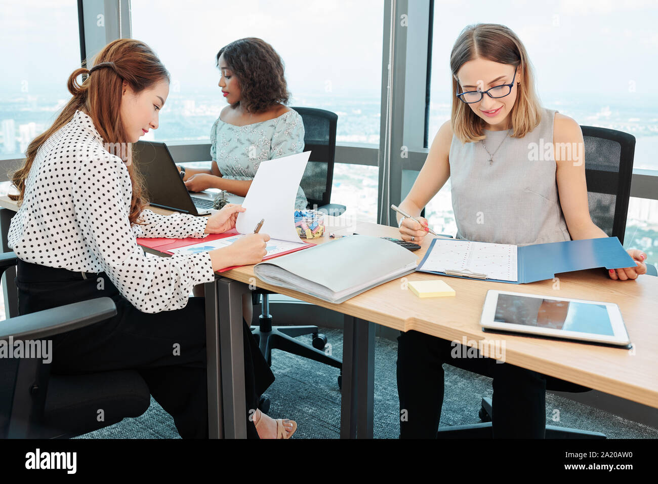 Team of female managers sitting at long office desk and examining ...