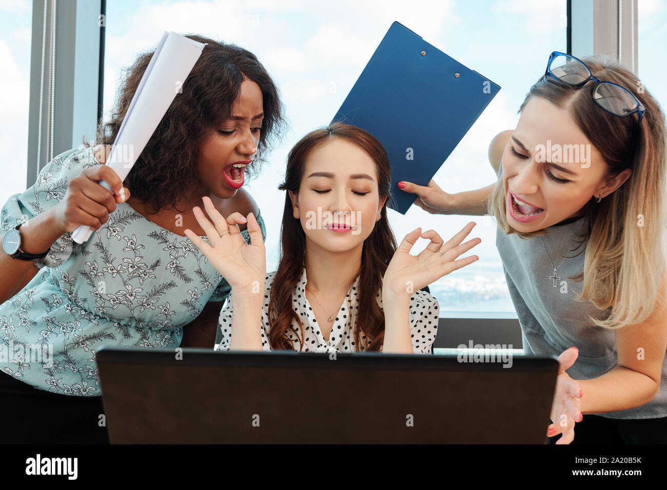 Pretty young Asian businesswoman sitting at desk with opened laptop and ...