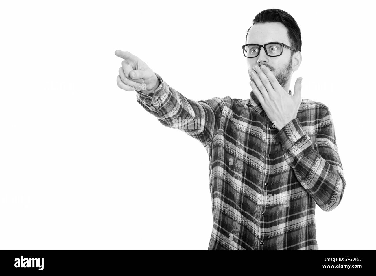 Studio shot of young man pointing at distance while looking shocked ...