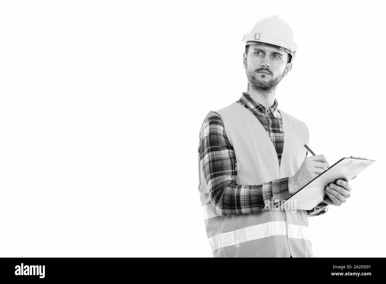 Studio shot of young man construction worker writing on clipboard while ...