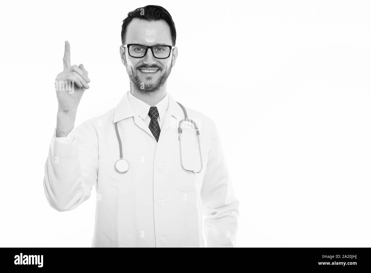 Studio shot of young happy man doctor smiling while pointing finger up ...
