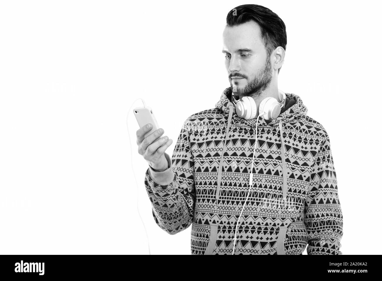 Studio shot of young man using mobile phone while wearing headphones ...