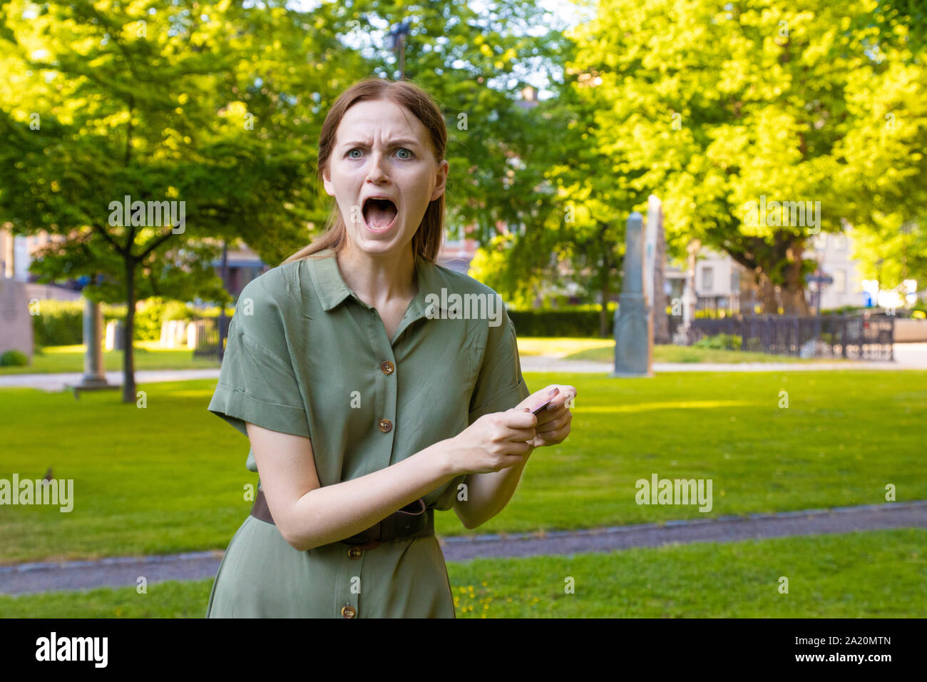 Young blonde indignant girl in a green dress with a credit card on a ...