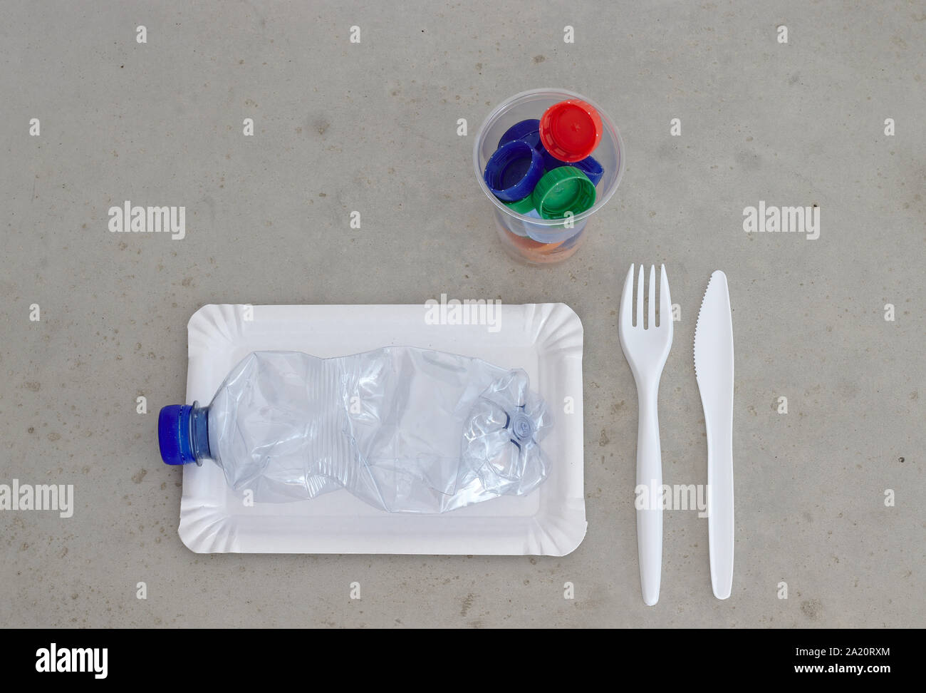 Plastic garbage on a plate, next to fork, spoon and cup filled with ...