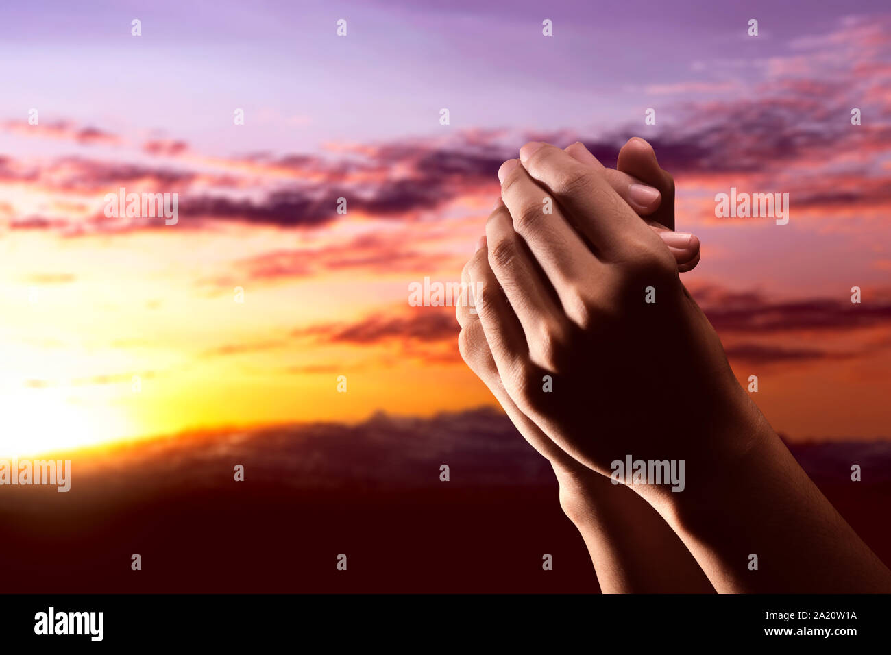 Human hands raised while praying to god with a sunset sky background ...