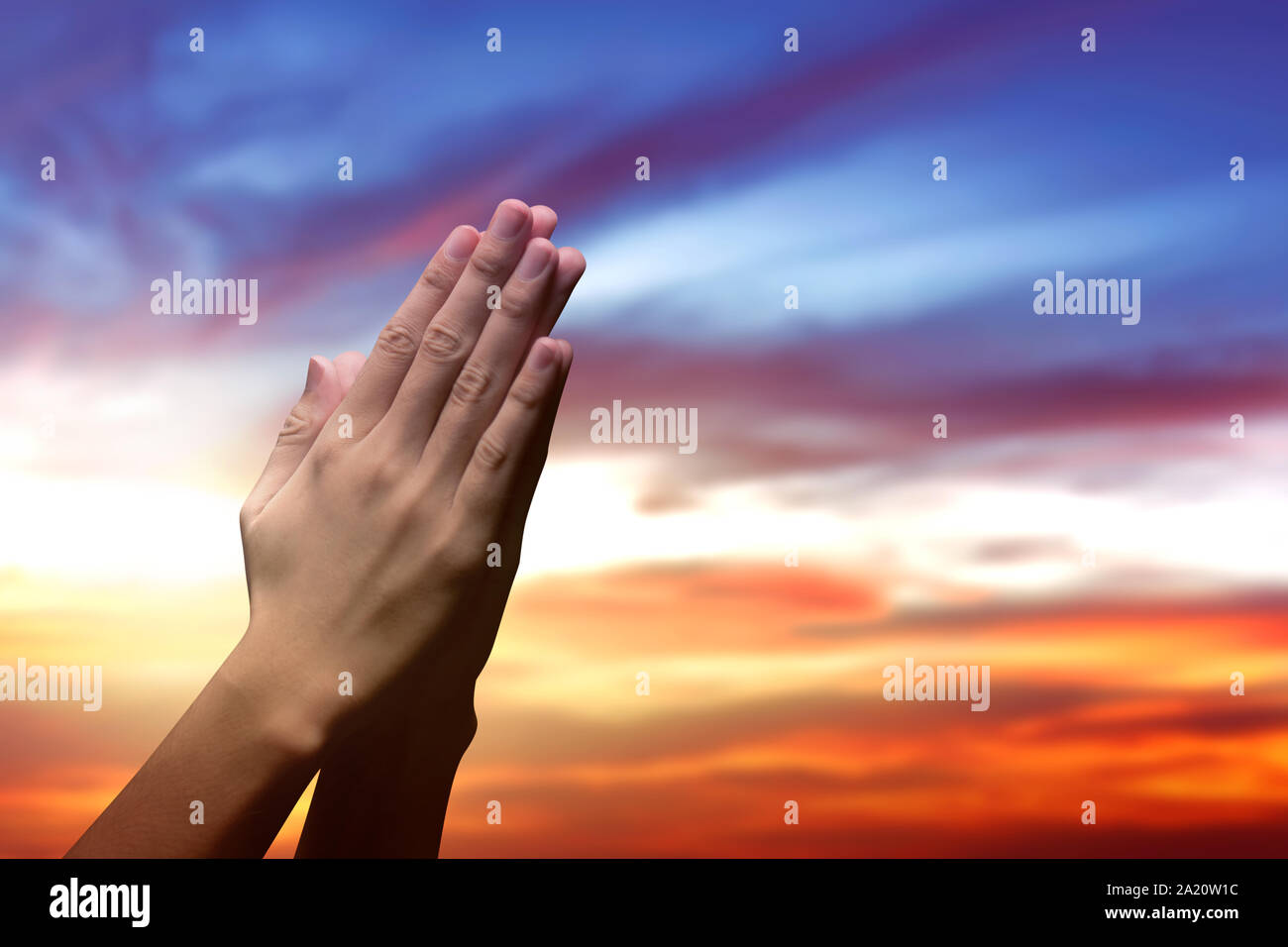 Human hands raised while praying to god with a sunset sky background ...