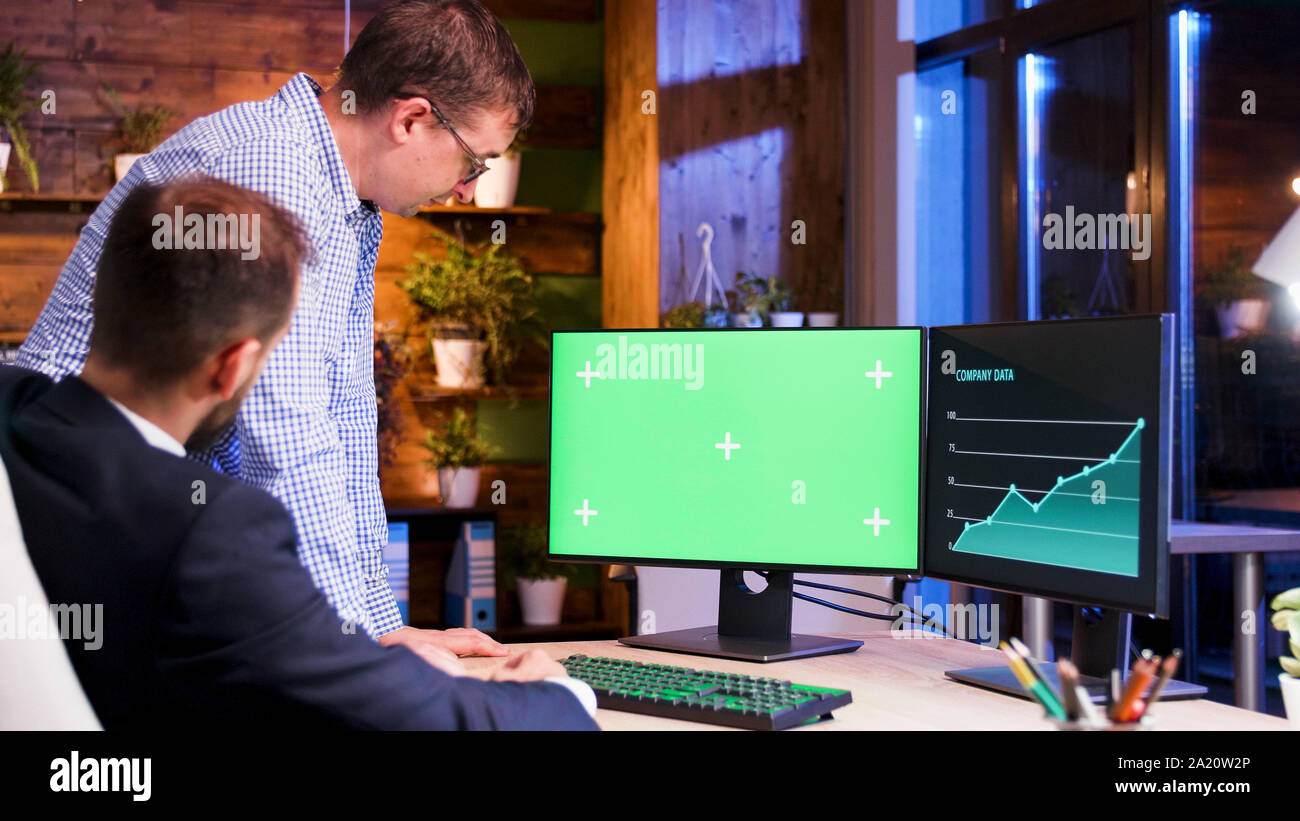 Two office colleagues looking at a green computer screen. Moon light ...