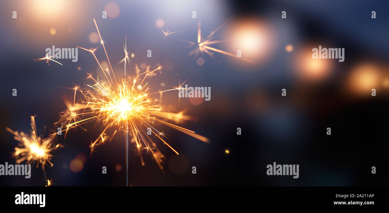 Glittering burning sparkler against blurred bokeh light background ...