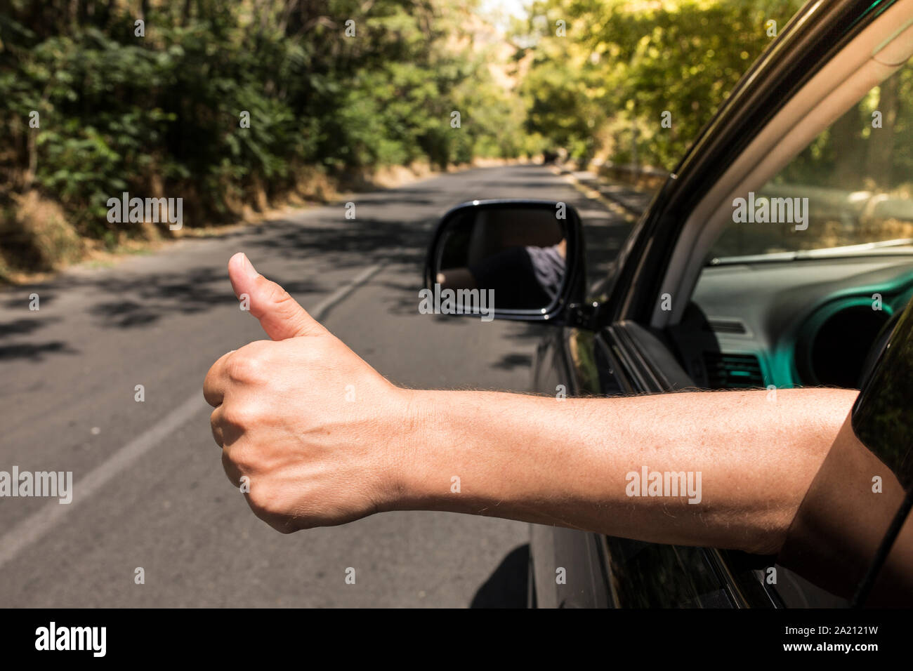 Young happy man drives a car and holds his hand out from the window ...