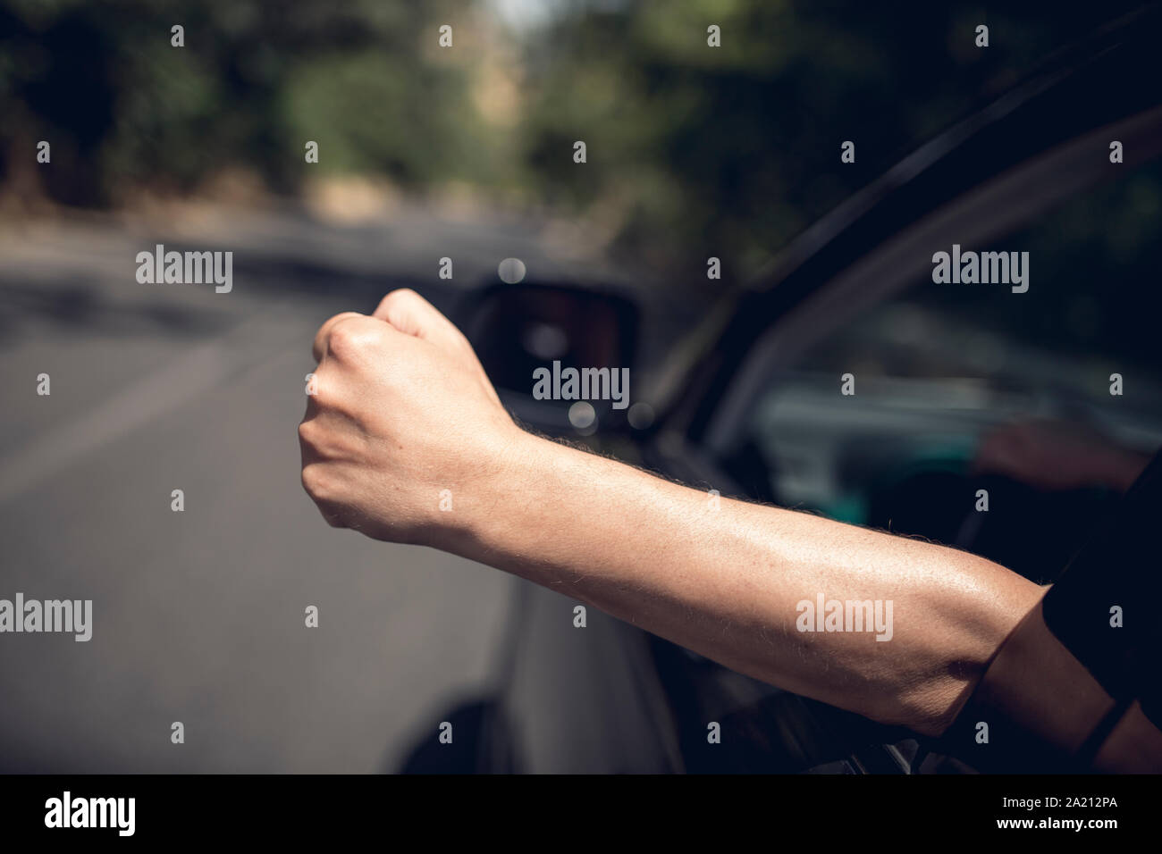 Young happy man drives a car and holds his hand out from the window ...
