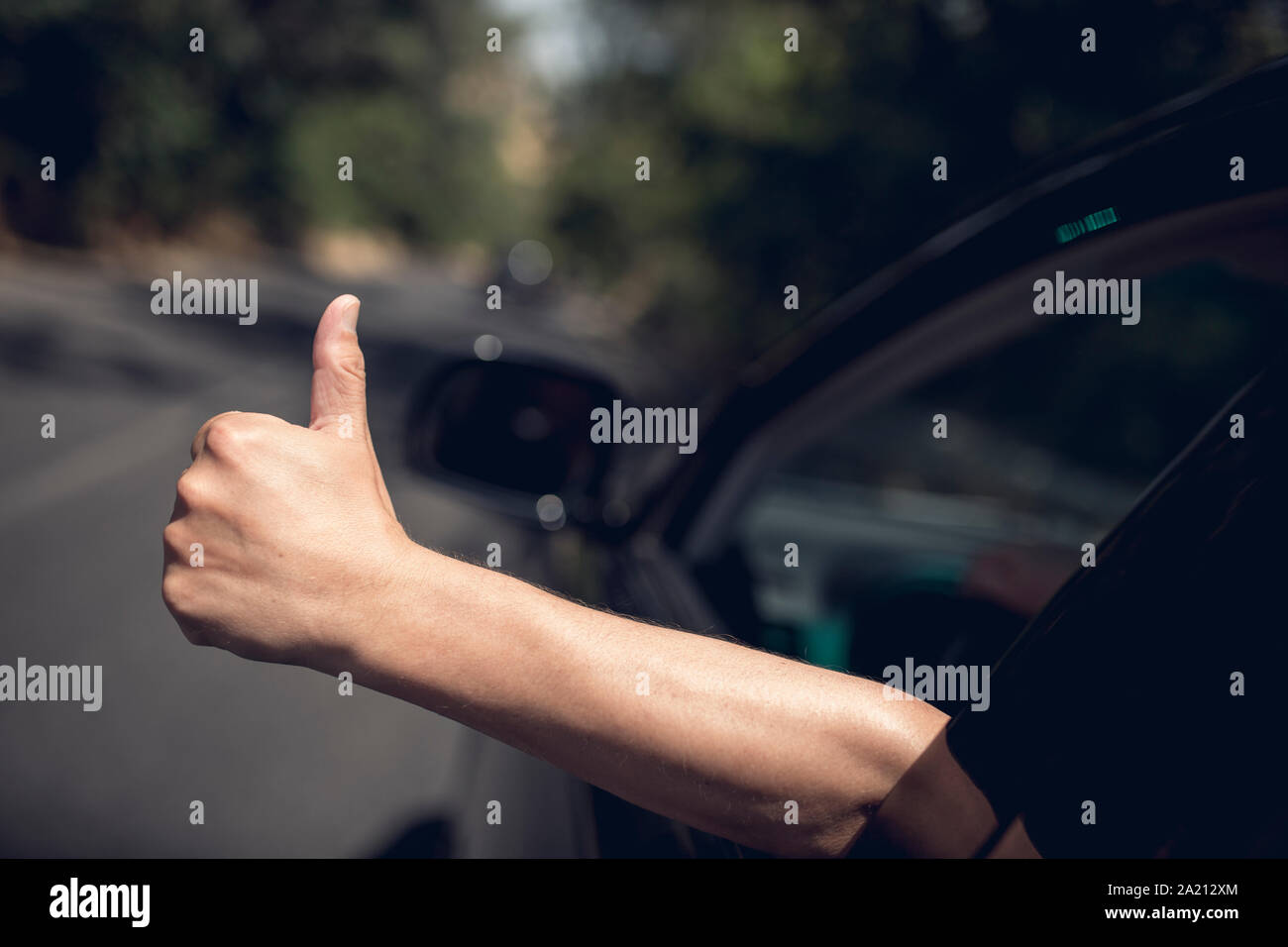 Young happy man drives a car and holds his hand out from the window ...
