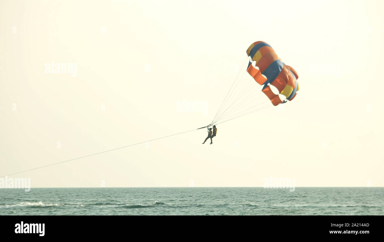 Couple flying with parachute over sea on summer day Stock Photo - Alamy