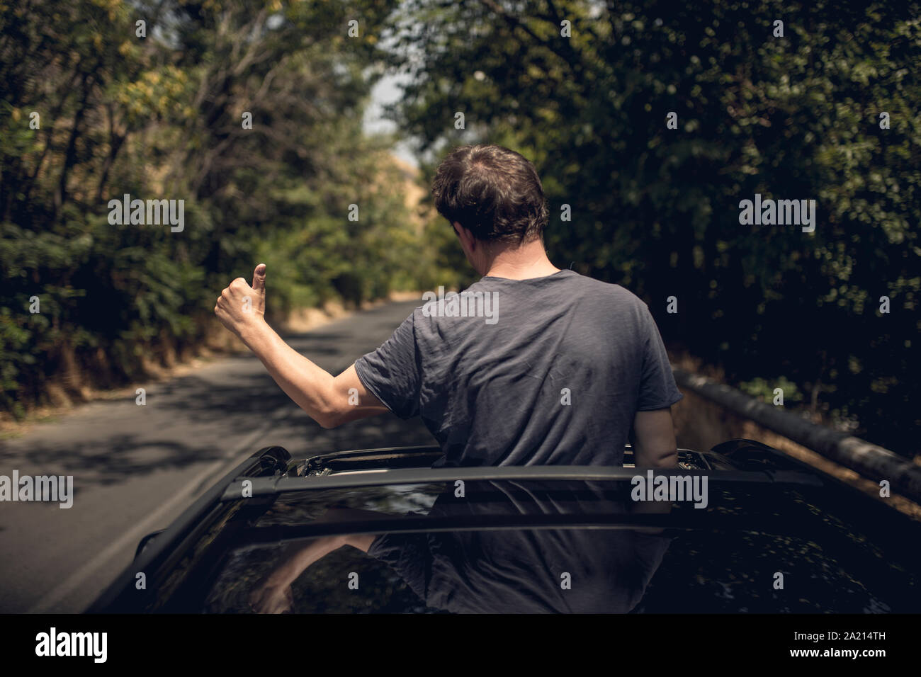 Young happy man drives a car and holds his hand out from the window ...