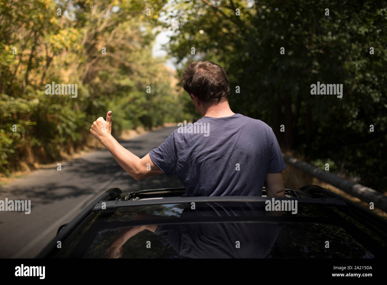 Young happy man drives a car and holds his hand out from the window ...
