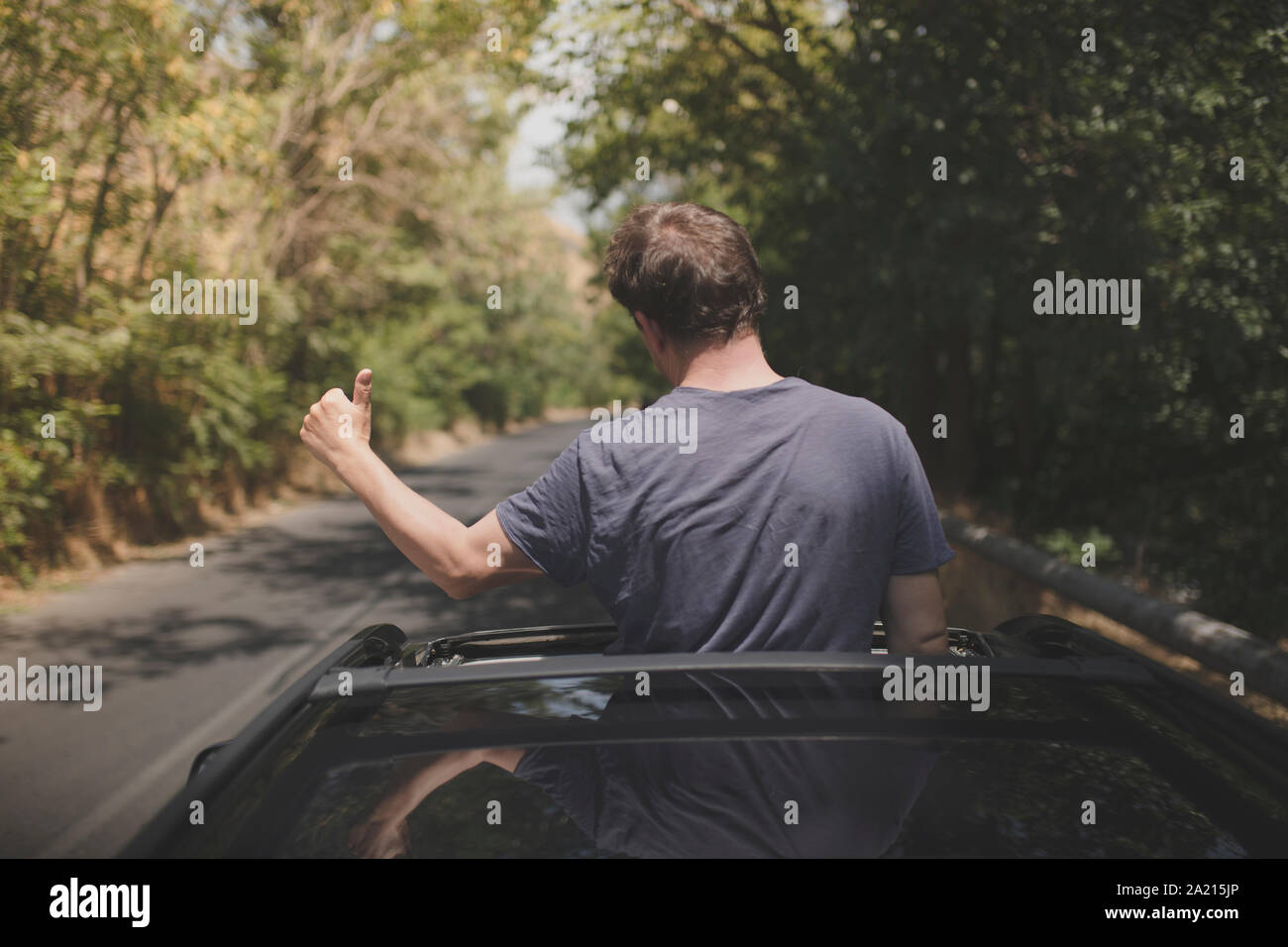 Young happy man drives a car and holds his hand out from the window ...