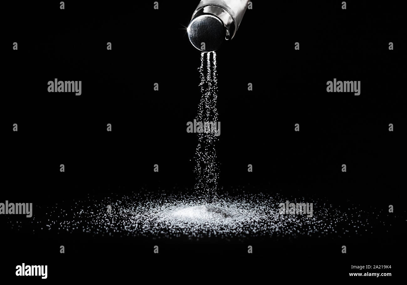 Salt spills out of the salt shaker in thin streams on a black ...
