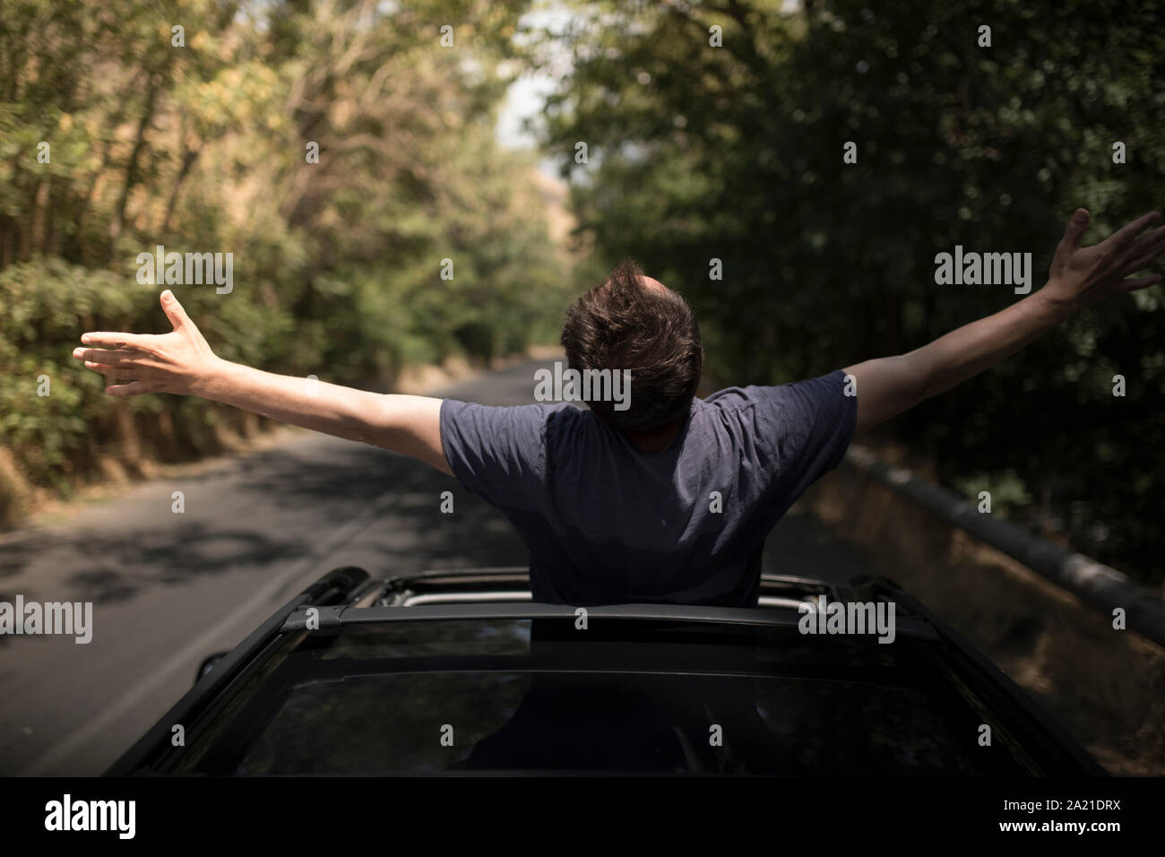 Young happy man drives a car and holds his hand out from the window ...
