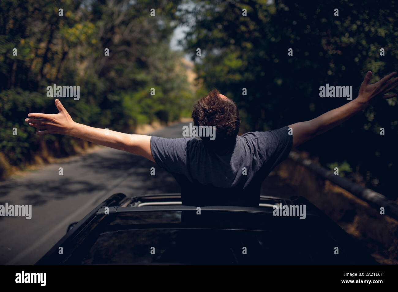 Young happy man drives a car and holds his hand out from the window ...