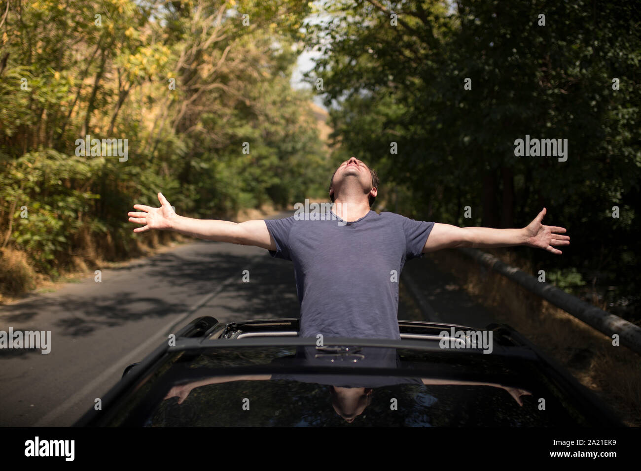 Young happy man drives a car and holds his hand out from the window ...