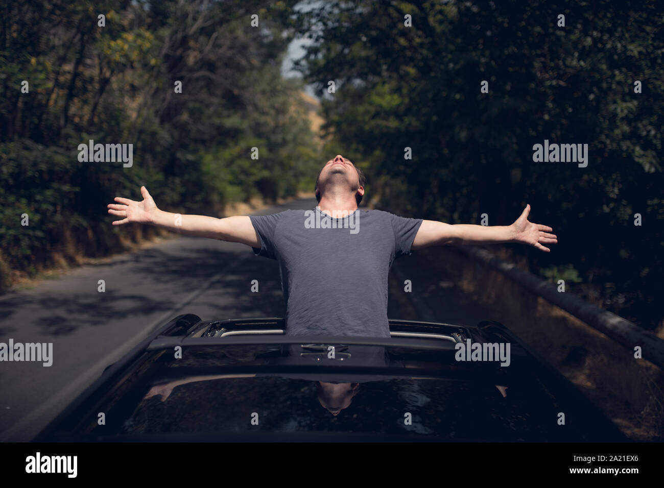 Young happy man drives a car and holds his hand out from the window ...