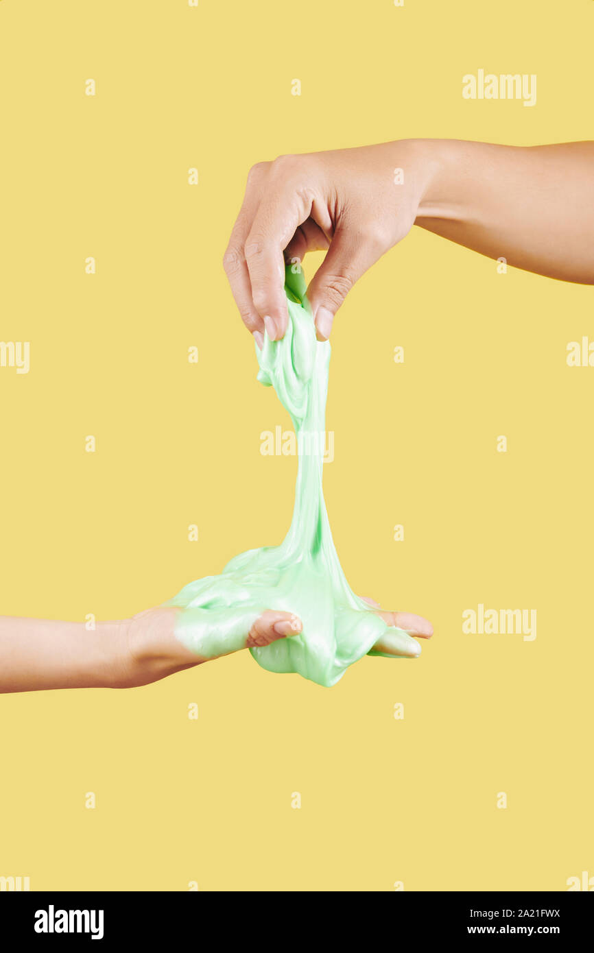 Person taking homemade green slime from hand of friend and pulling it ...