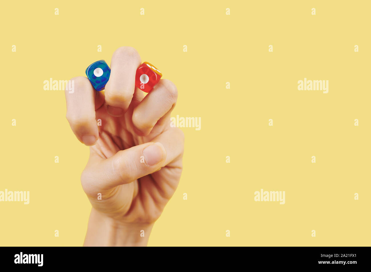 Hand of person with red and blue dice between fingers on yellow ...