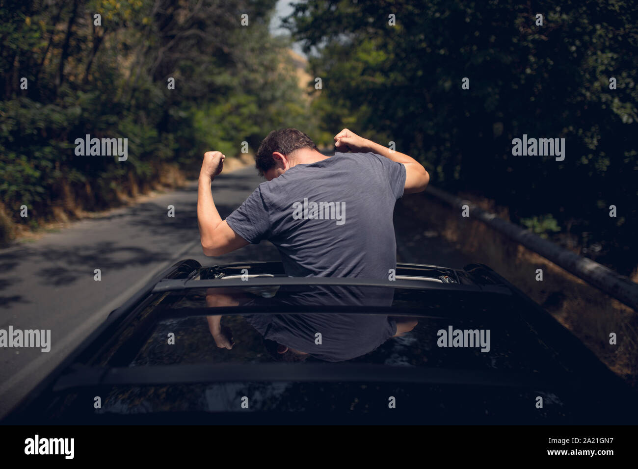 Young happy man drives a car and holds his hand out from the window ...