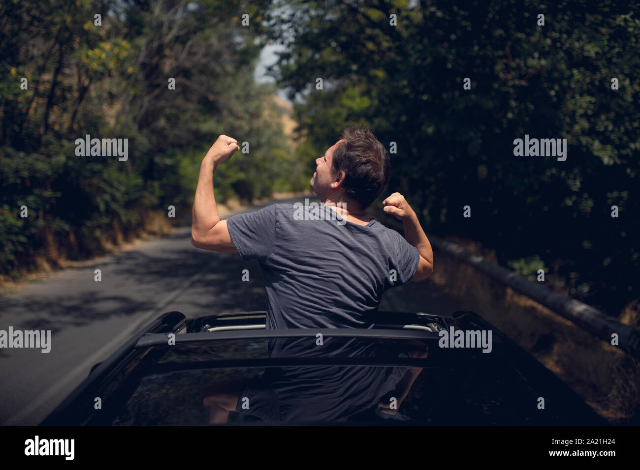 Young happy man drives a car and holds his hand out from the window ...