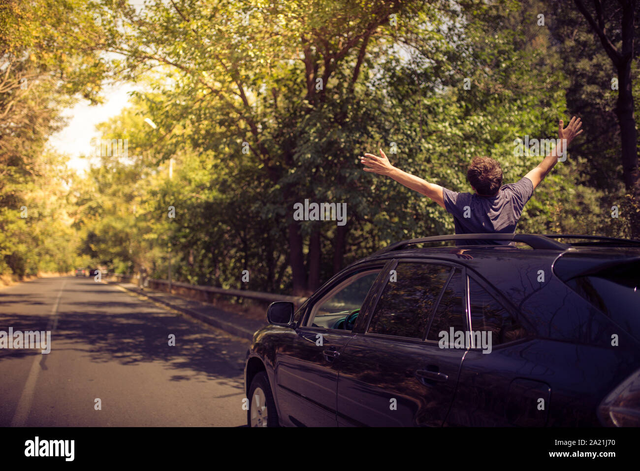 Young happy man drives a car and holds his hand out from the window ...