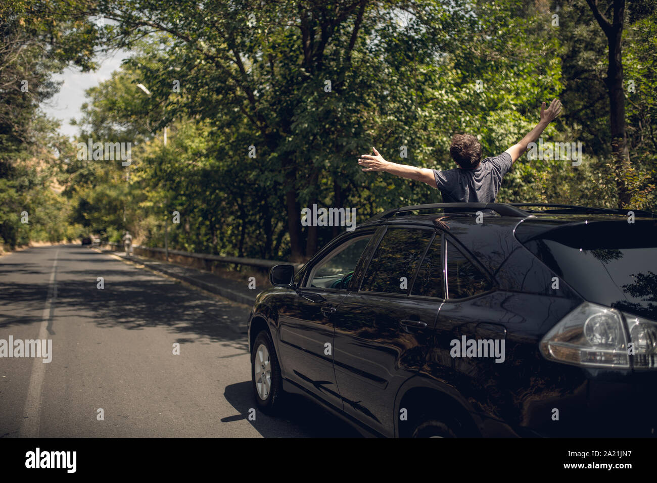 Young happy man drives a car and holds his hand out from the window ...