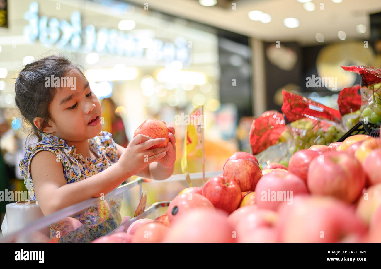 asian Little girl choosing a apple in a food store or a supermarket ...