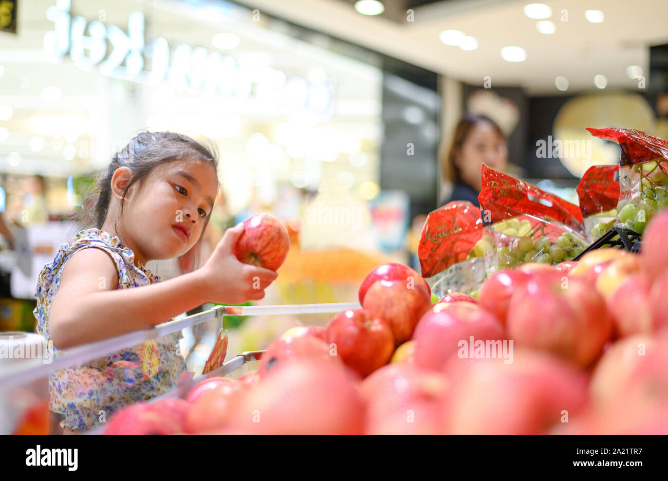 asian Little girl choosing a apple in a food store or a supermarket ...