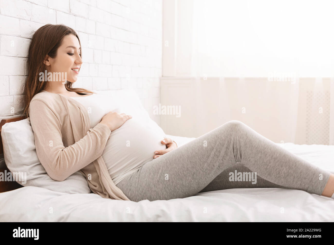 Happy pregnancy. Young expectant woman touching her belly, enjoying her ...