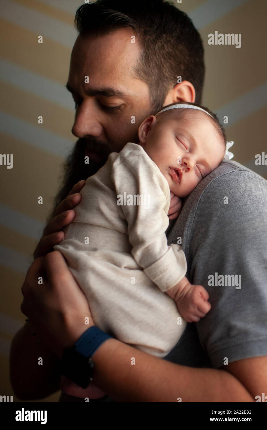 Newborn baby girl sleeping on father's shoulder at home in soft light ...