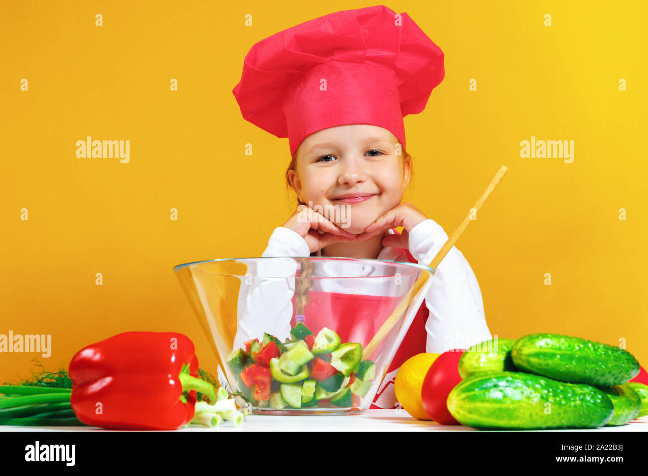 Beautiful little girl chef cook on a yellow background. A child is ...