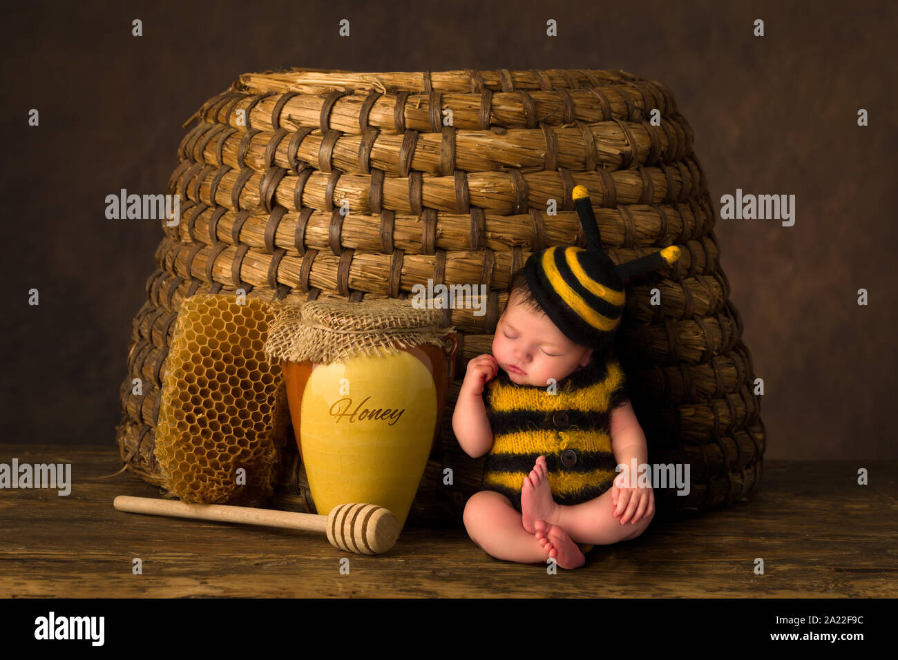 Sleepy cute baby in bee outfit resting against an antique beehive Stock ...