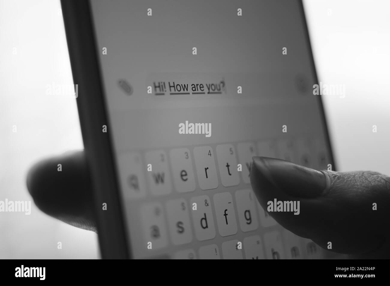 Human hand typing on a white smartphone a message Hi, how are you. BW ...