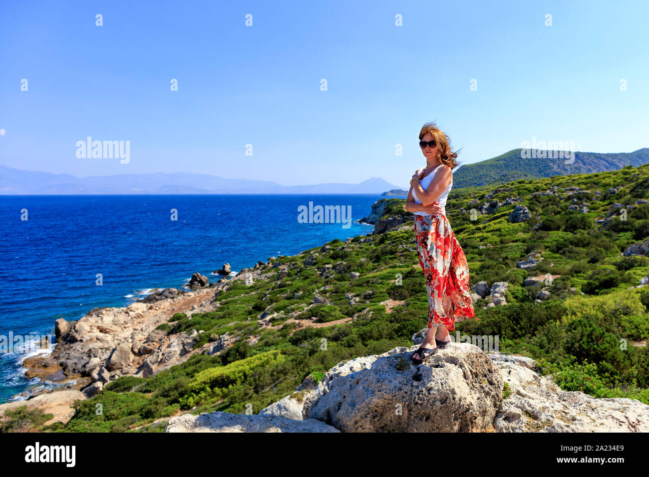 A beautiful lady stands in the wind on a large stone boulder against ...