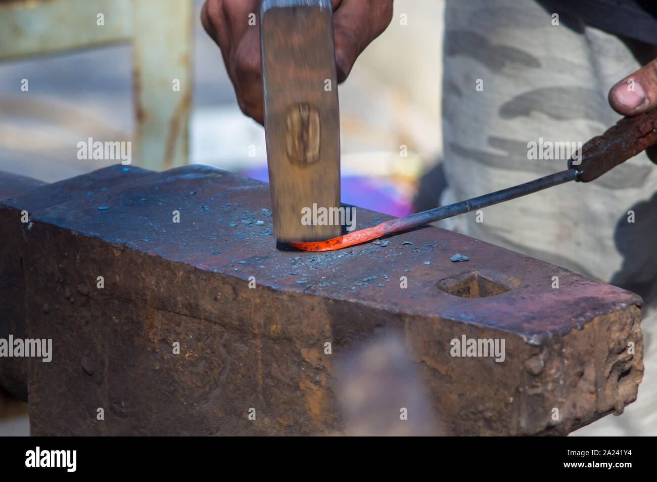 blacksmith performs the forging of hot glowing metal on the anvil ...