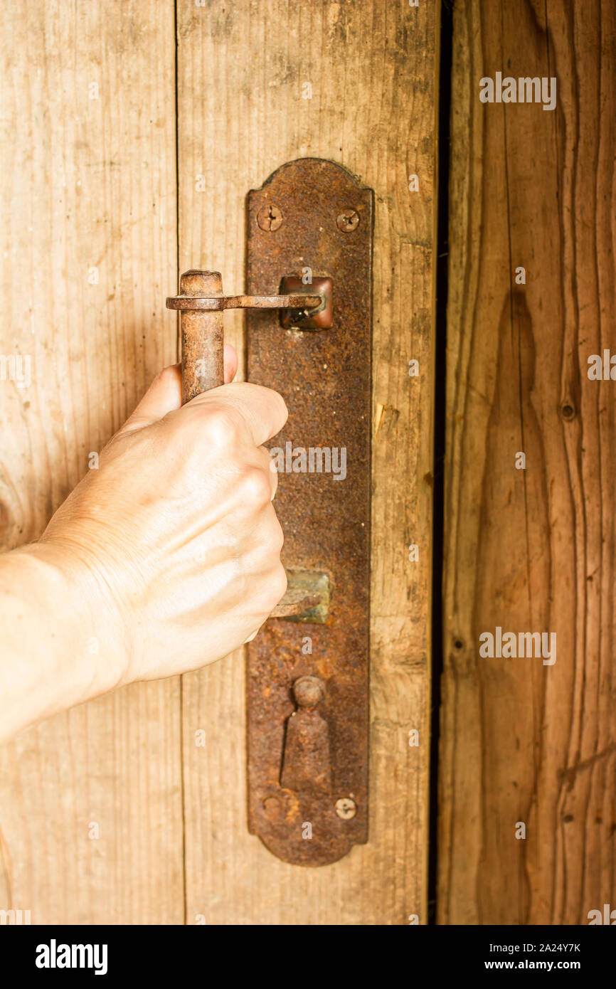 A person opens the wooden door by hand using of an old rusty handle ...