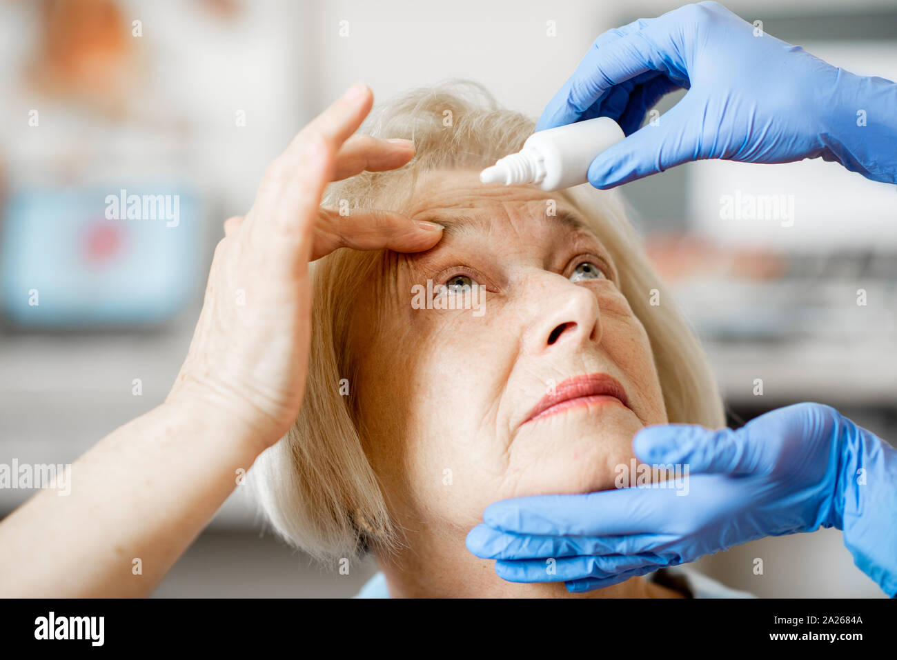 Doctor or nurse in medical gloves dripping eye drops on eyes of a ...