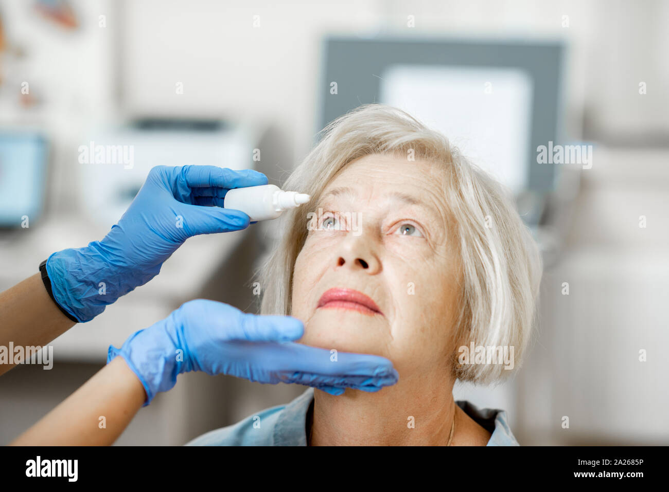 Doctor dripping eye drops on eyes of a senior patient during a ...
