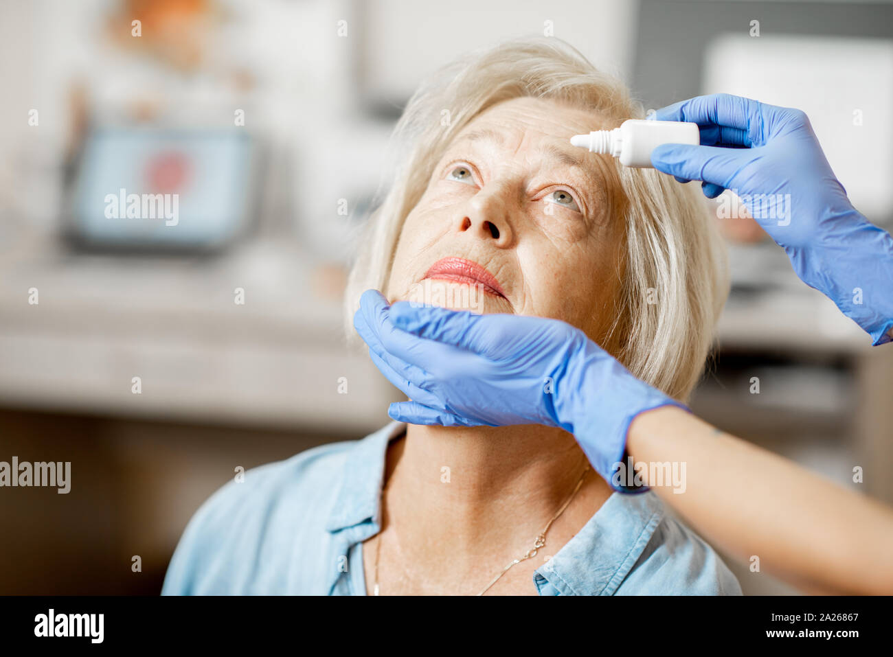 Doctor or nurse in medical gloves dripping eye drops on eyes of a ...