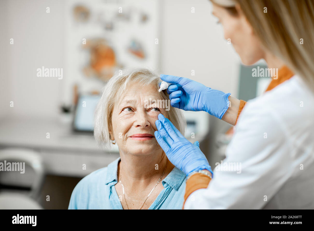 Female doctor dripping eye drops on eyes of a senior patient during a ...