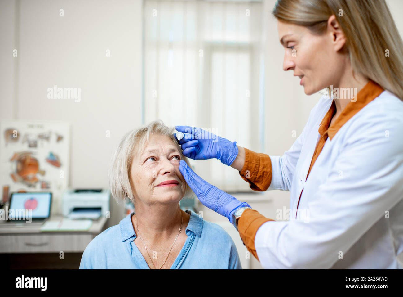 Female doctor dripping eye drops on eyes of a senior patient during a ...