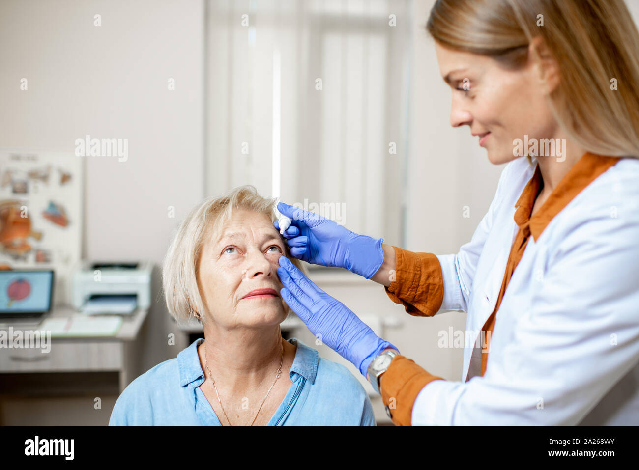 Female doctor dripping eye drops on eyes of a senior patient during a ...