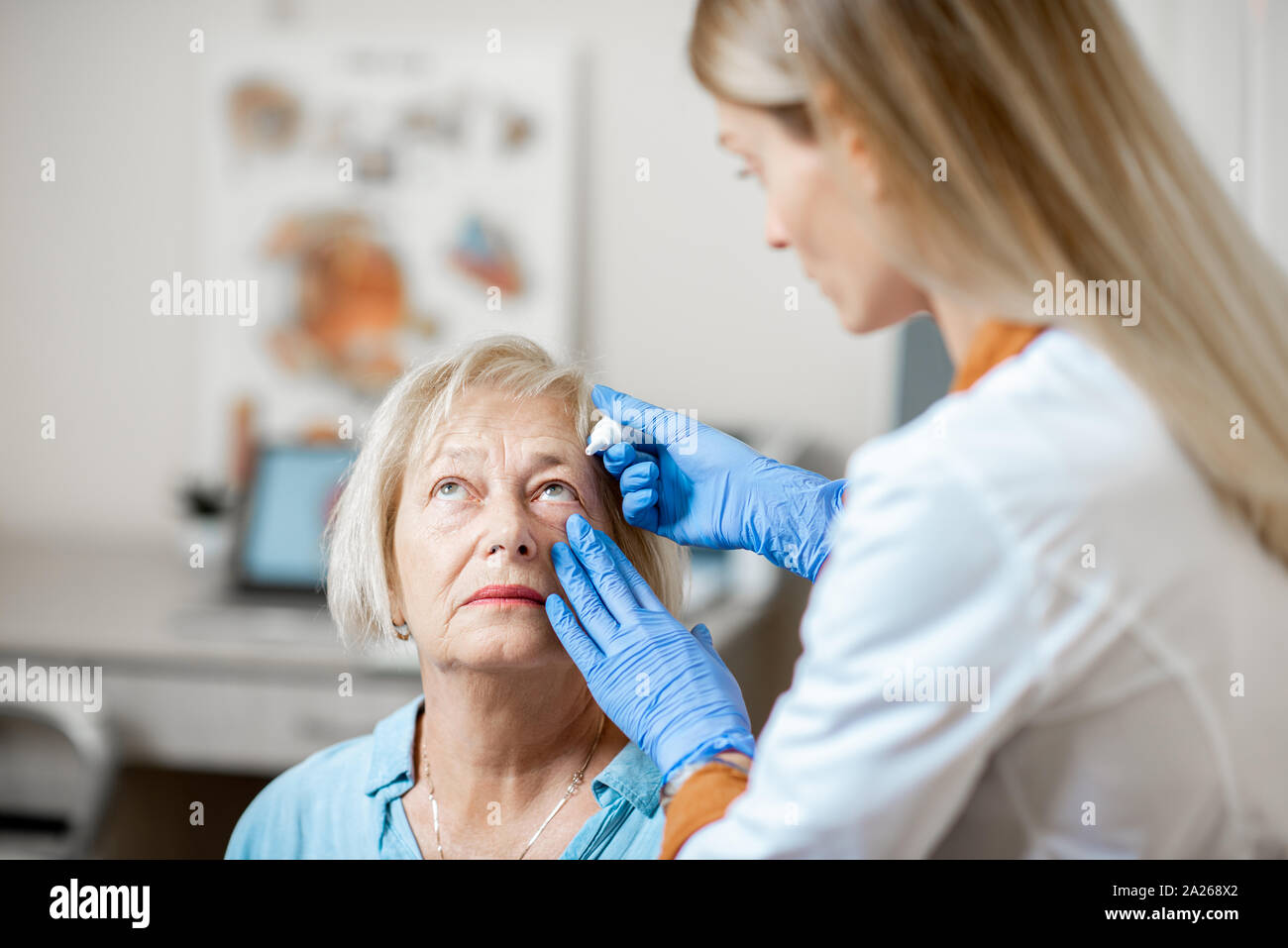 Female doctor dripping eye drops on eyes of a senior patient during a ...