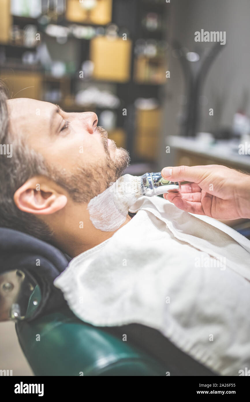 Fashionable man client during beard shaving in barber shop Stock Photo ...